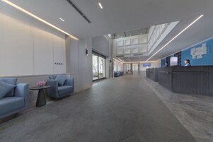 Um hall amplo com balcão de recepção, área de estar e teto alto com claraboias.