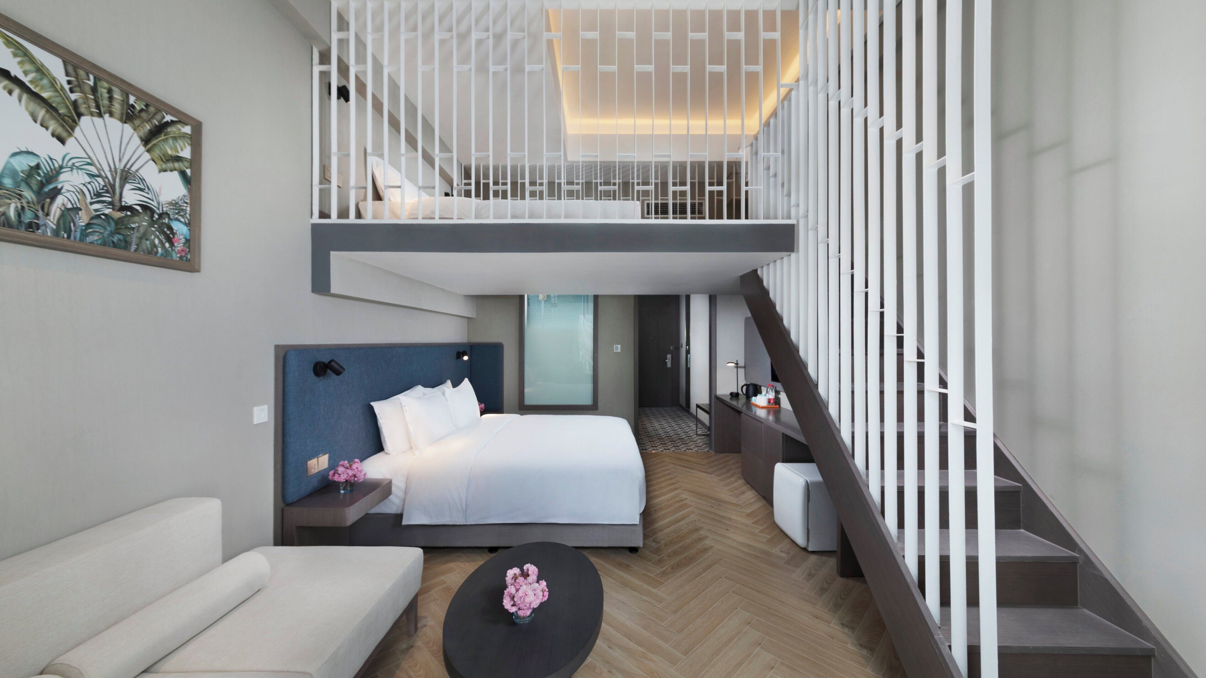 Quarto de hotel moderno com cama, sofá, mesa de centro e escada.