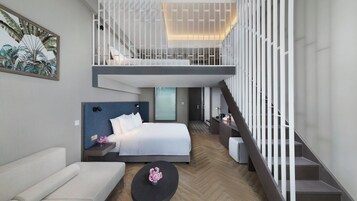 Quarto de hotel moderno com cama, sofá, mesa de centro e escada.