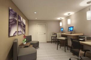 Quarto de hotel com escrivaninha, duas cadeiras, computador, impressora e porta.