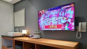 Uma casa de banho moderna com toucador de madeira, espelho, televisão e telefone.