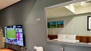 Um banheiro de hotel com um espelho grande, pia, televisão e um armário de toucador de madeira.