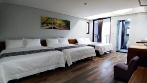 Quarto de hotel com três camas, piso de madeira, uma escrivaninha e uma cadeira.