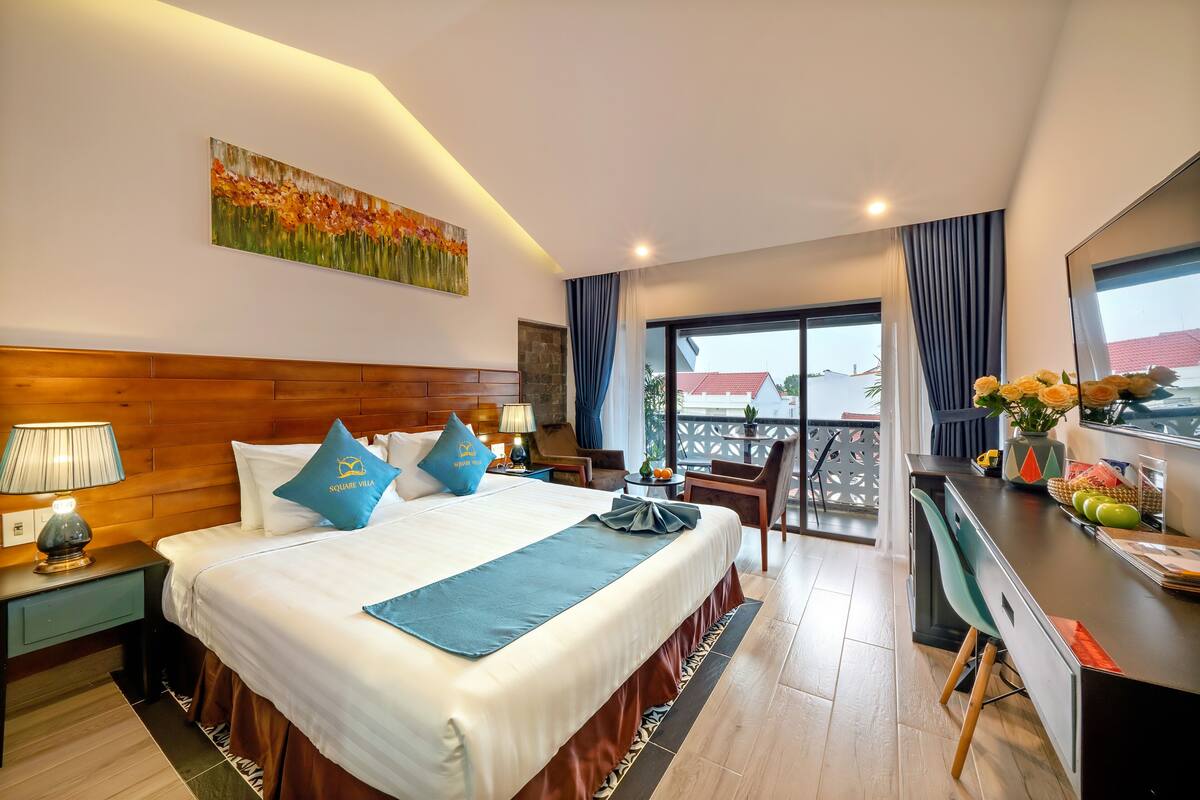Quarto de hotel com cama grande, escrivaninha, varanda com vista e um quadro na parede.