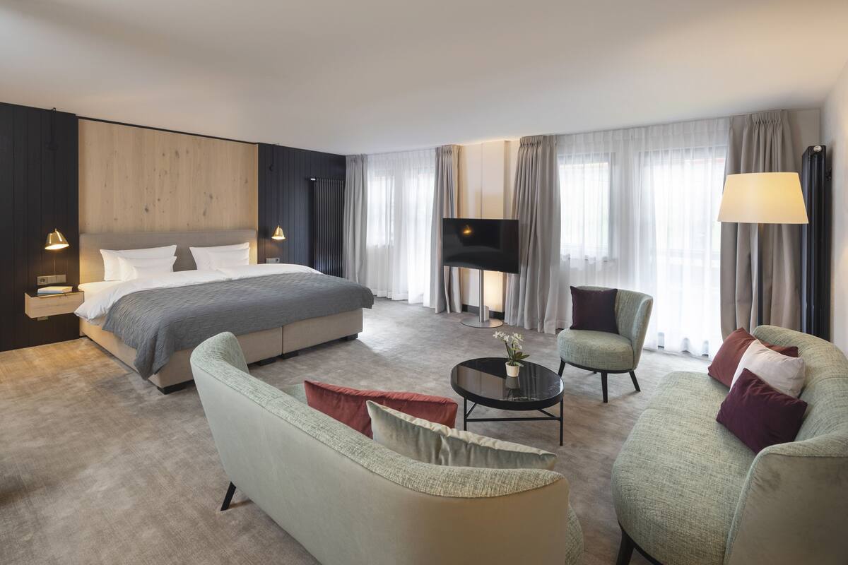 Quarto de hotel moderno com uma cama grande, um sofá, uma mesinha e uma televisão.