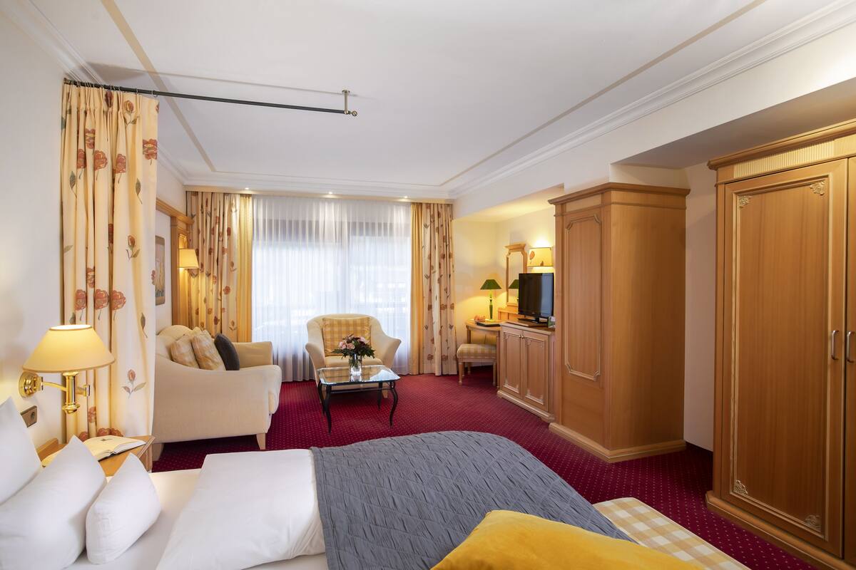 Quarto de hotel com cama grande, sofá, escrivaninha com abajur, televisão e guarda-roupa.