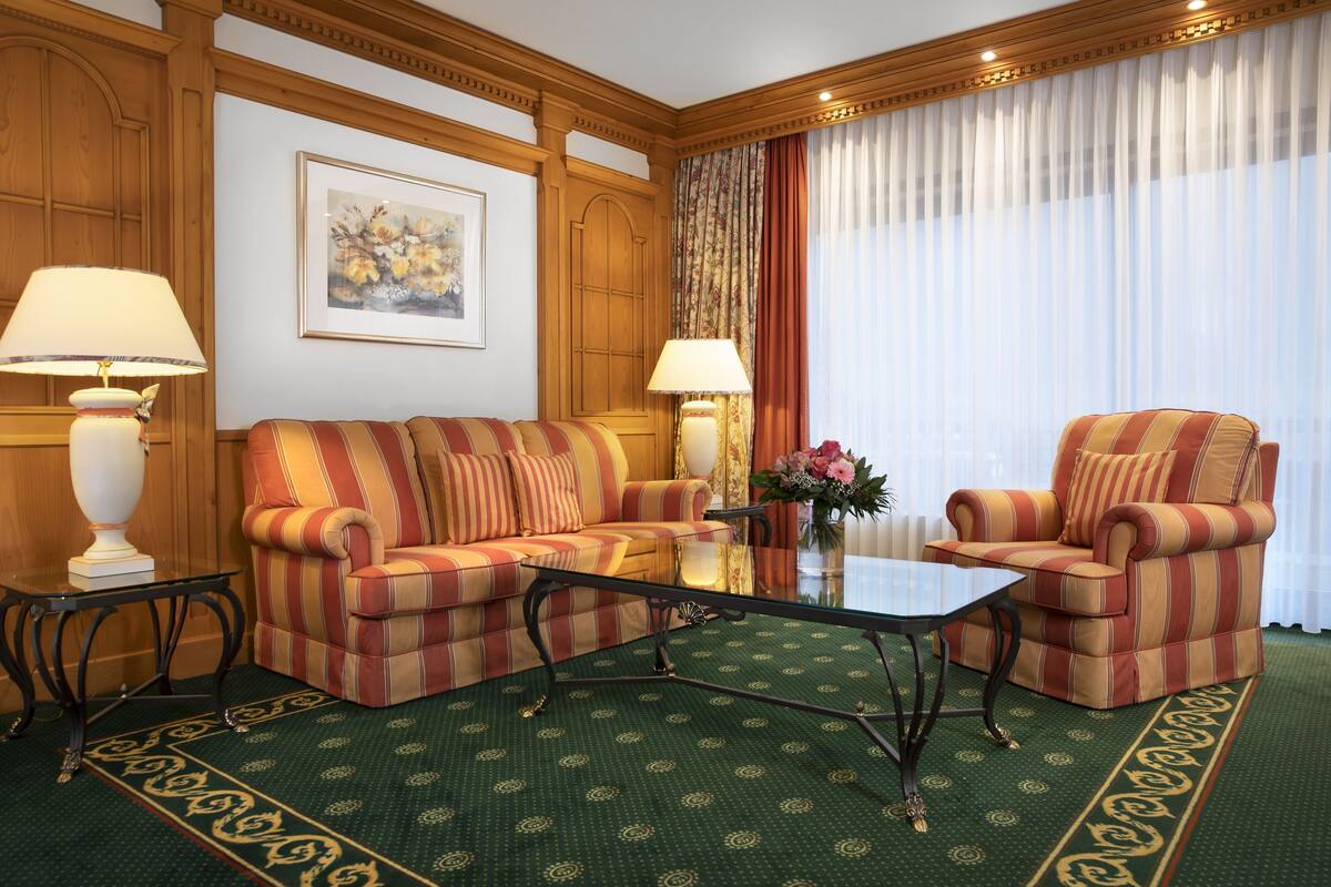 Um quarto com um sofá listrado, poltronas, uma mesa de centro de vidro e duas luminárias.
