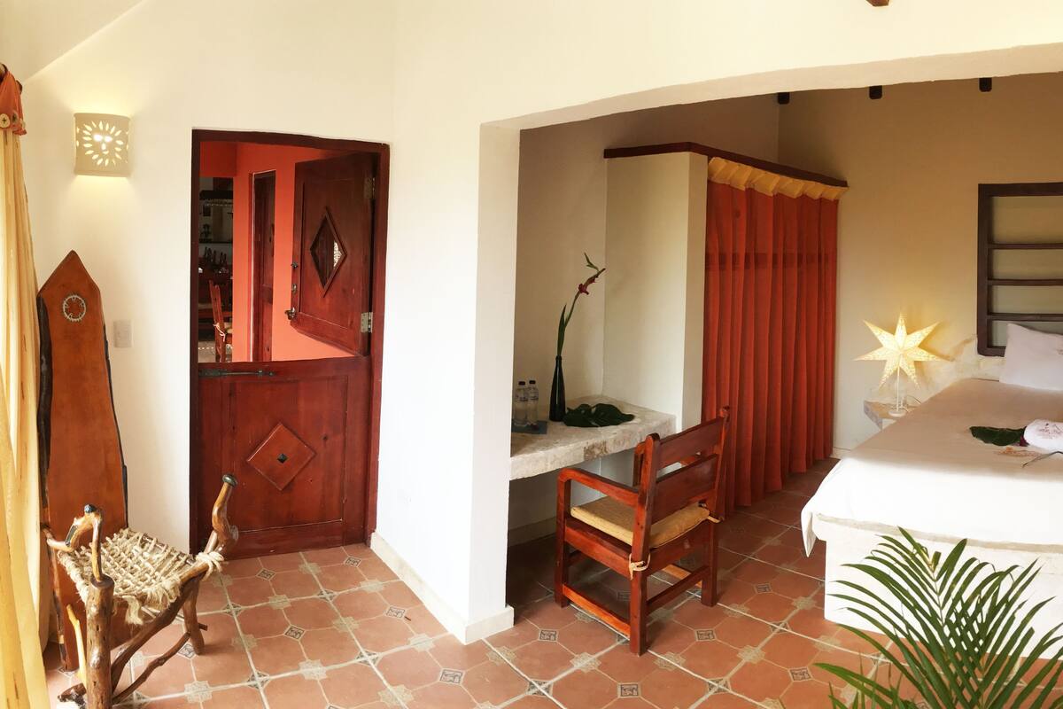 Quarto com cama, escrivaninha, cadeira, mesa de cabeceira e janela com cortinas.
