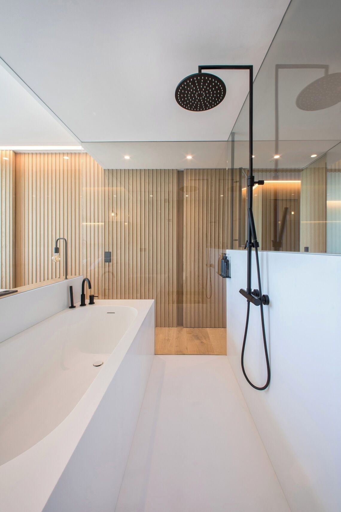Uma casa de banho moderna com uma banheira branca grande, um chuveiro preto e painéis de madeira nas paredes.