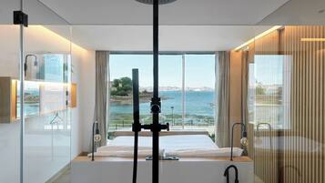 Quarto de hotel moderno com uma cama grande, um chuveiro e vista para o mar.