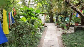 Um caminho de pedra ladeado por vegetação exuberante e plantas em vasos, que leva a um muro de pedra.