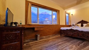 Quarto com cama de madeira, uma escrivaninha com computador e janela com vista para as montanhas.