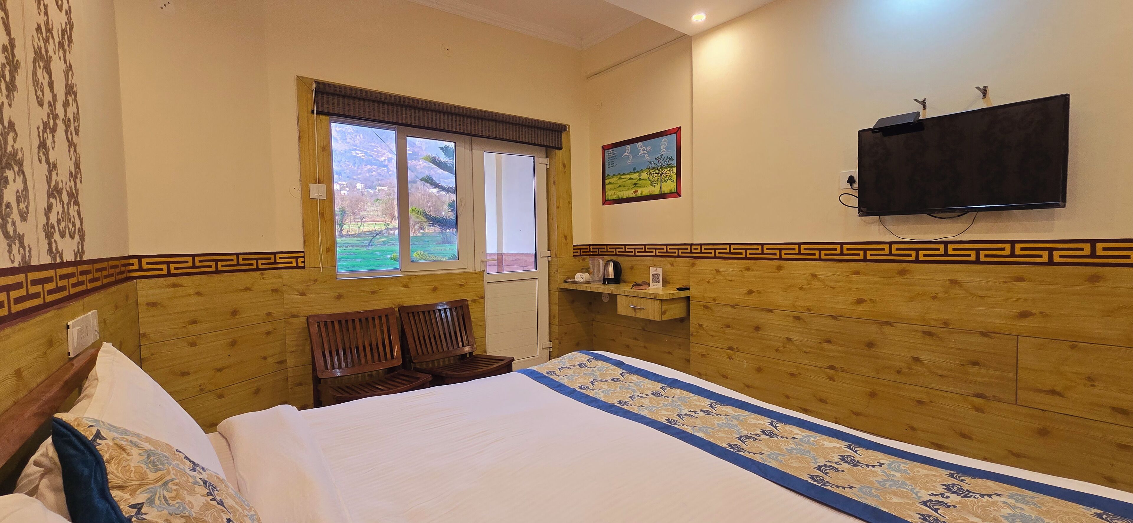 Quarto de hotel com cama, cabeceira de madeira, janela com vista, televisão na parede e um pequeno móvel com chaleira.