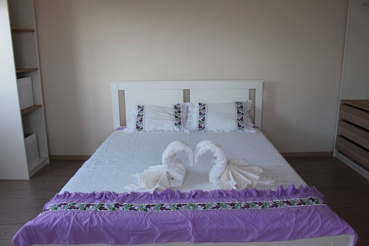 Uma cama bem arrumada com colcha roxa e almofadas decorativas.