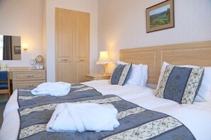 Quarto de hotel com duas camas, um guarda-roupa de madeira, uma mesa de cabeceira com abajur e um quadro na parede.