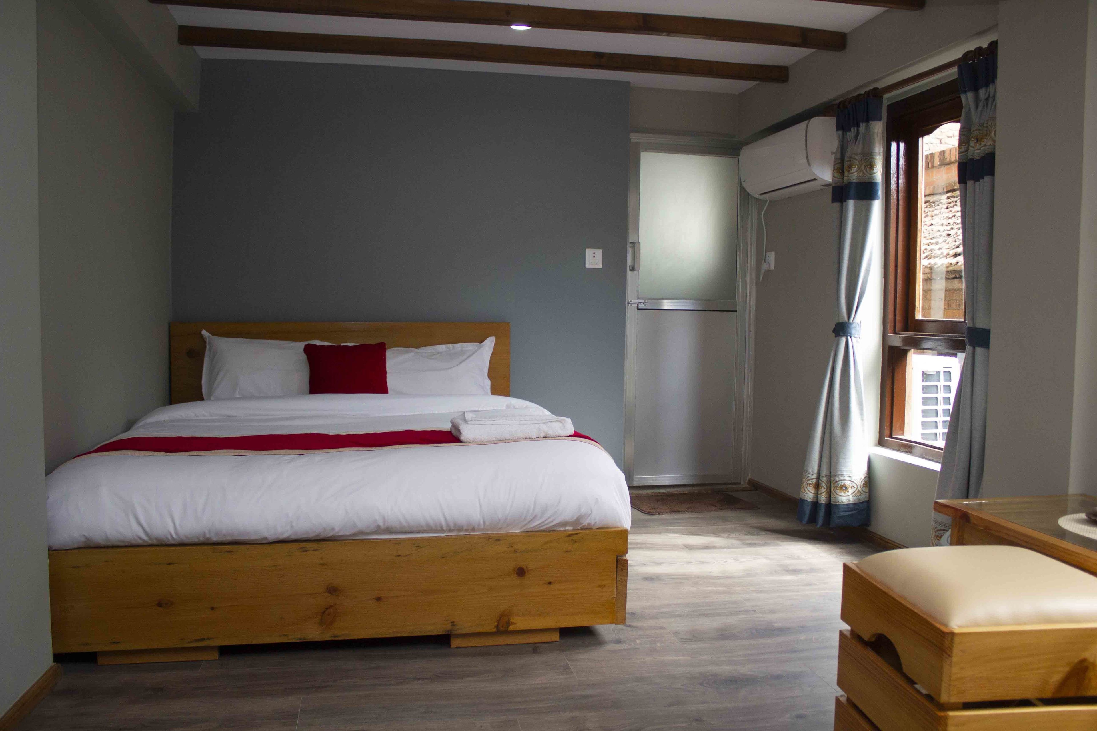 Quarto com cama de madeira, almofada vermelha, cobertor branco e um banquinho de madeira.