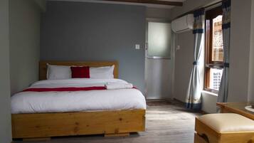 Quarto com cama de madeira, almofada vermelha, cobertor branco e um banquinho de madeira.