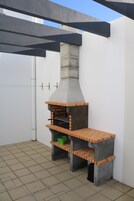 Forno de tijolos ao ar livre com chaminé, soalho em azulejos e parede branca ao fundo.