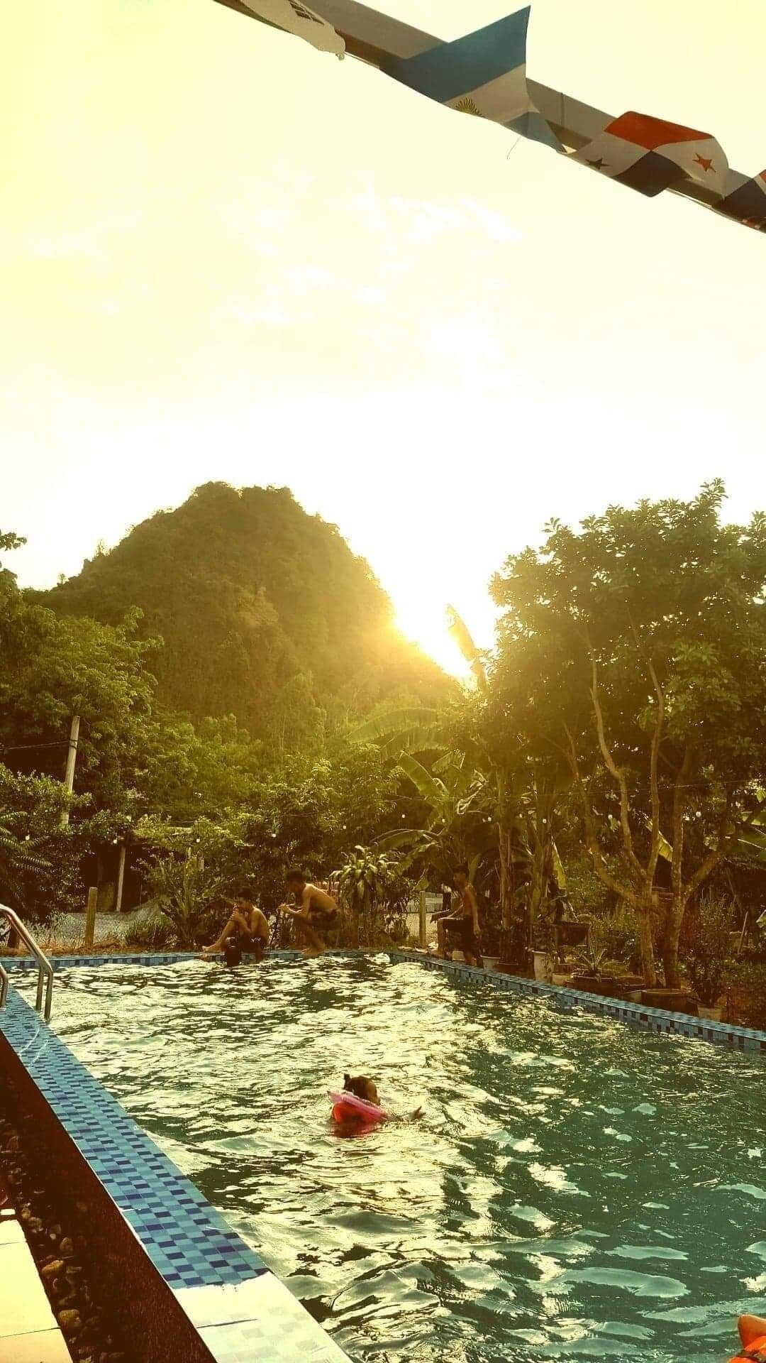 Piscina com uma pessoa na água, cercada por vegetação exuberante e uma colina ao fundo.