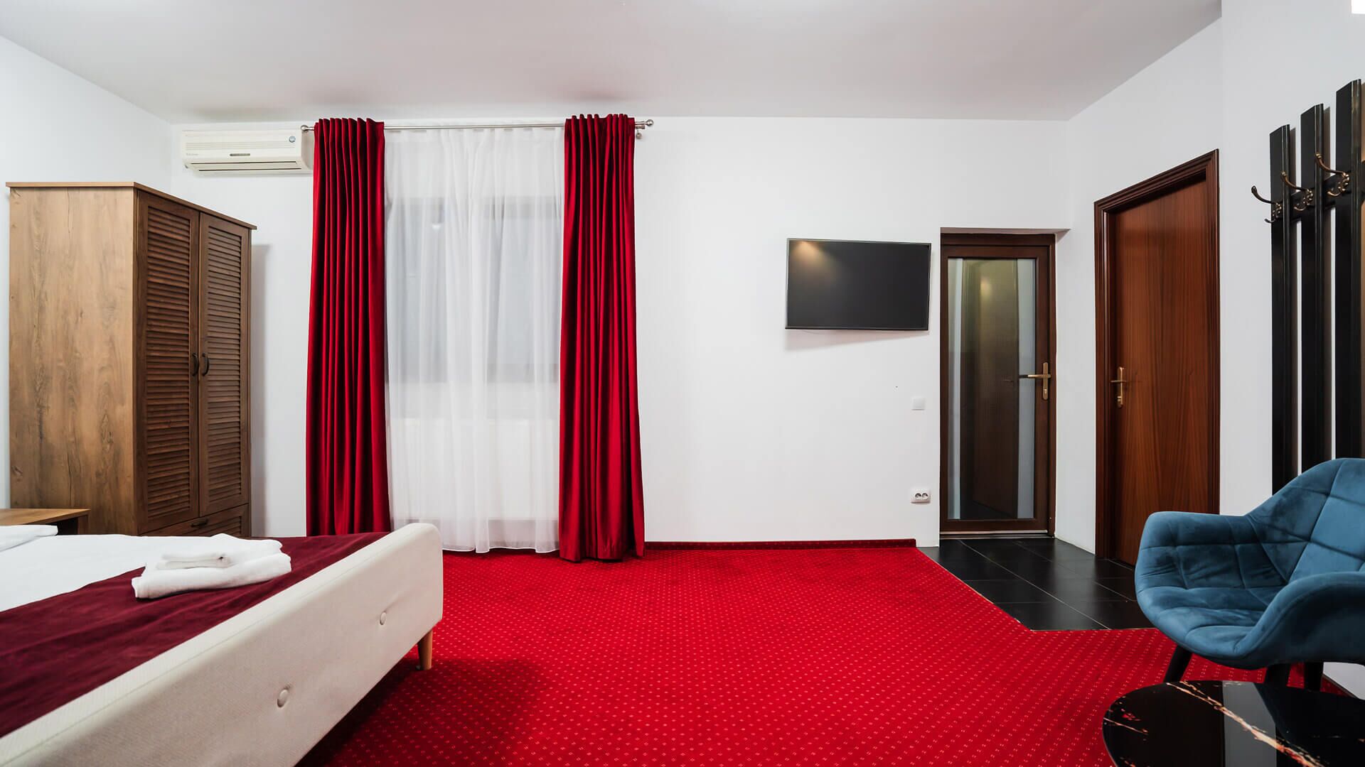 Quarto de hotel com uma cama, televisão, guarda-roupa, porta e uma cadeira azul.
