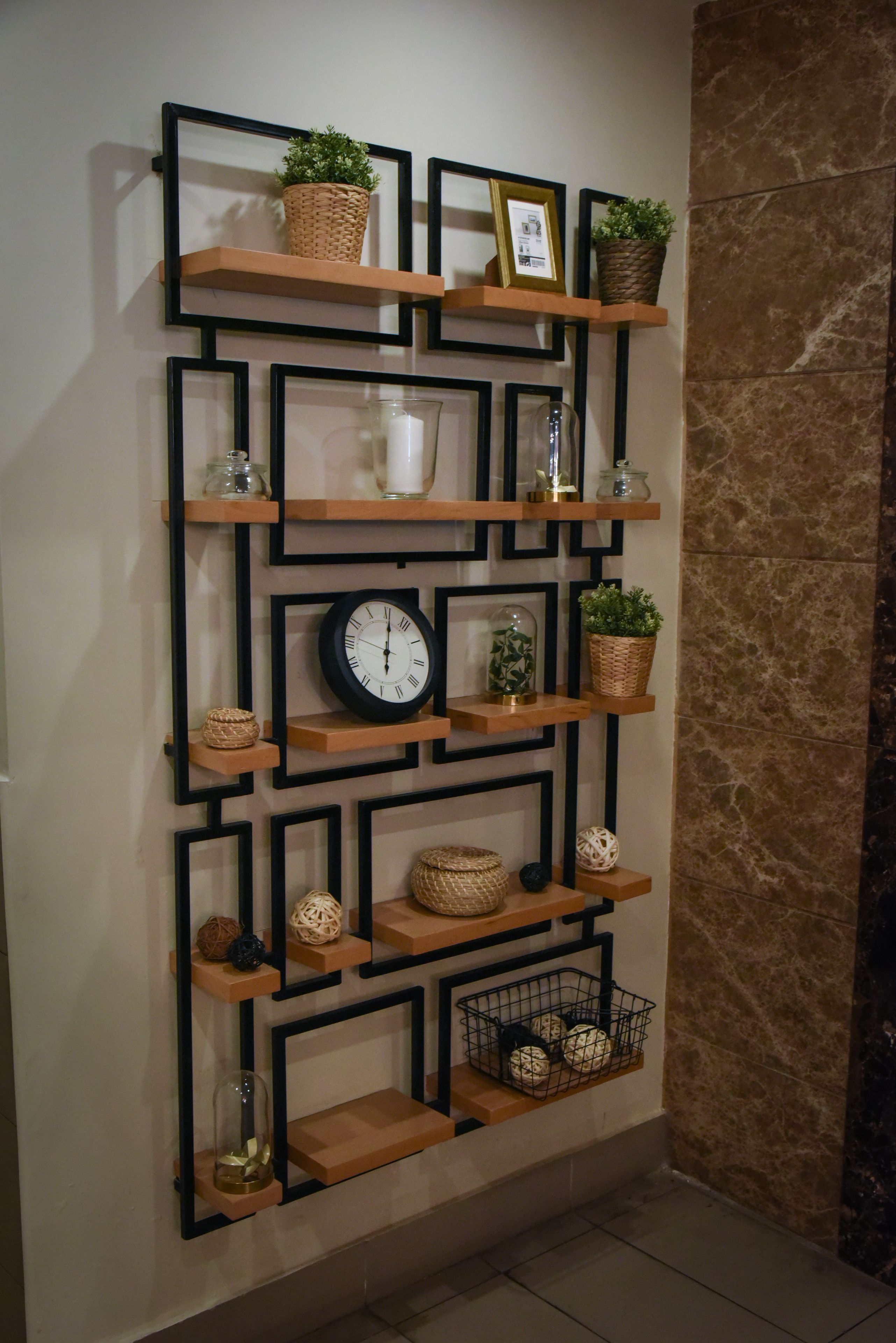 Uma estante fixa na parede com vários compartimentos, alguns contendo objetos decorativos como cestos e um relógio.