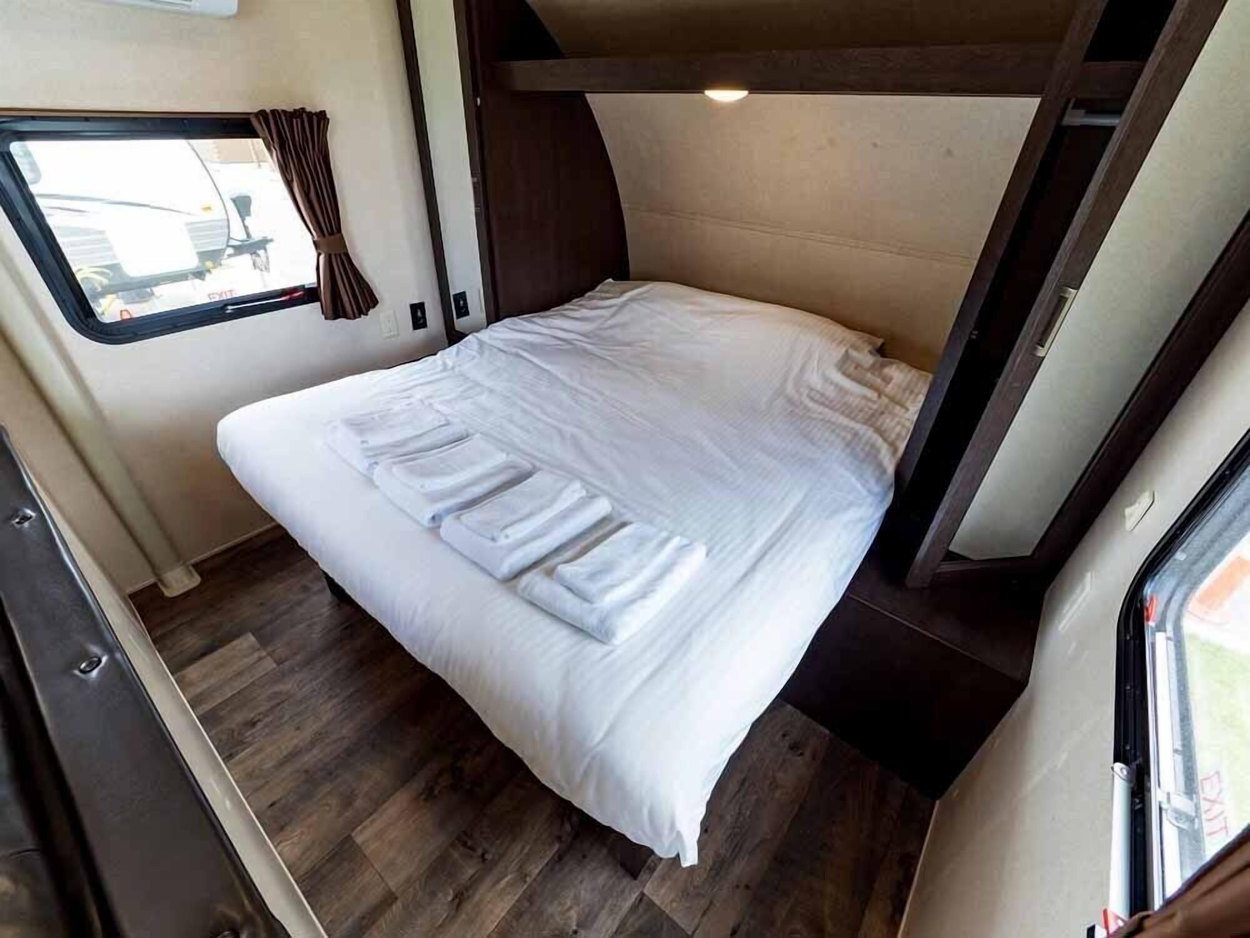 Cama compacta com lençóis brancos impecavelmente dobrados num pequeno quarto de motorhome.