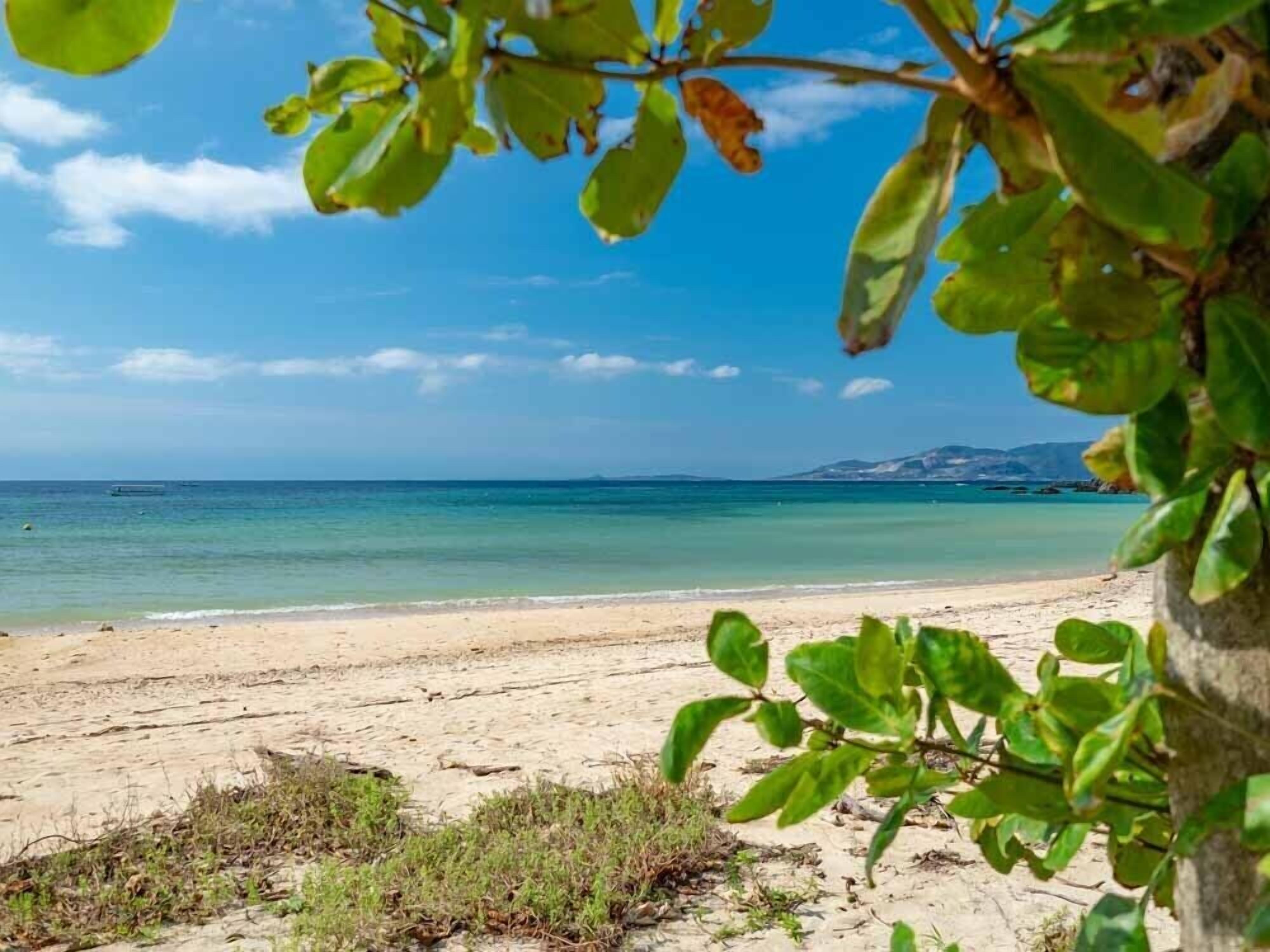 Uma praia com águas azul-claras, areal arenoso e montanhas ao longe.