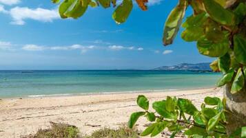 Uma praia com águas azul-claras, areal arenoso e montanhas ao longe.
