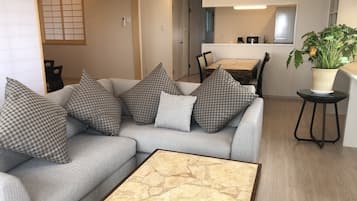 Uma sala de estar com um sofá cinza, almofadas estampadas, uma mesa de centro de madeira e um vaso com planta.