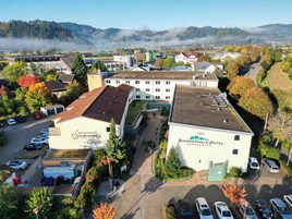 Hotel com estacionamento, rodeado por árvores e montanhas ao fundo.