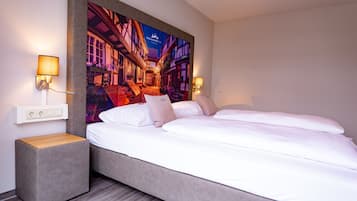 Quarto de hotel com uma cama grande, duas mesas de cabeceira e um quadro na parede retratando uma cena urbana.