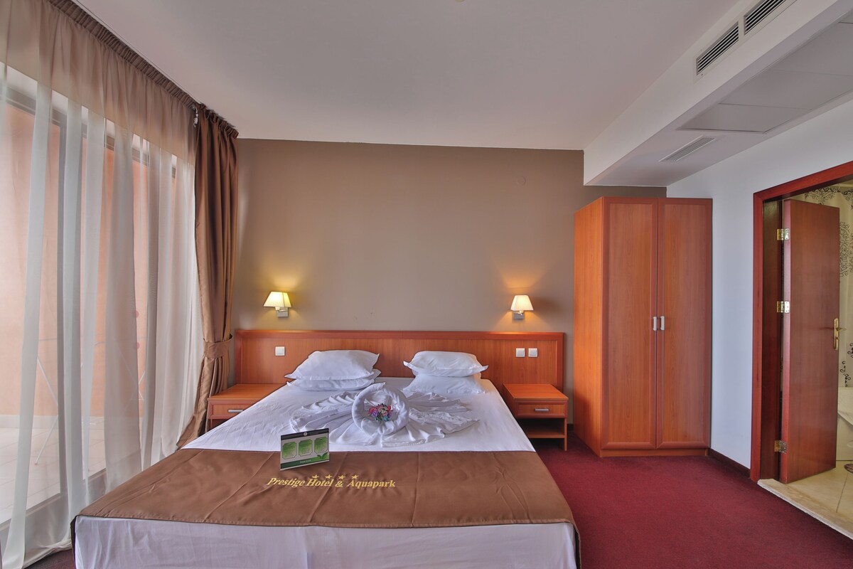 Quarto de hotel com cama, duas mesas de cabeceira, um guarda-roupa e uma porta.