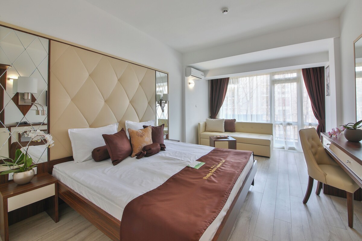 Quarto de hotel com uma cama grande, escrivaninha, sofá e televisão.