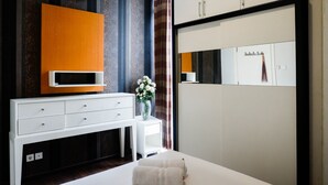 Quarto de hotel moderno com uma cama grande, cômoda branca, televisão e espelho.