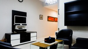 Uma sala de estar moderna com uma TV de tela plana, um armário branco, uma mesa de centro de vidro e uma poltrona de couro preto.