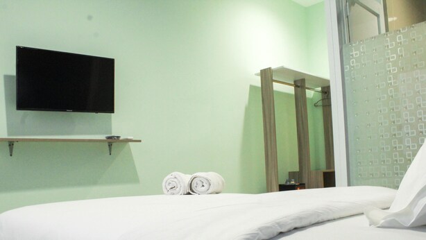 Quarto de hotel com cama, TV de tela plana na parede e área de chuveiro com portas de vidro jateado.