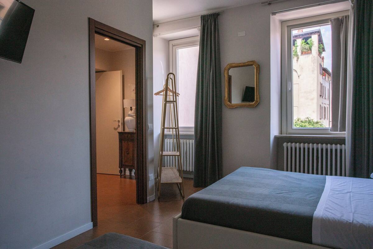 Quarto com cama, janela com cortinas, radiador e espelho na parede.