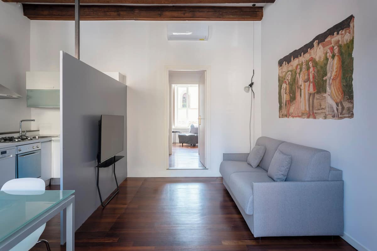 Um espaço de estar moderno com cozinha, um sofá cinzento e um quadro na parede.
