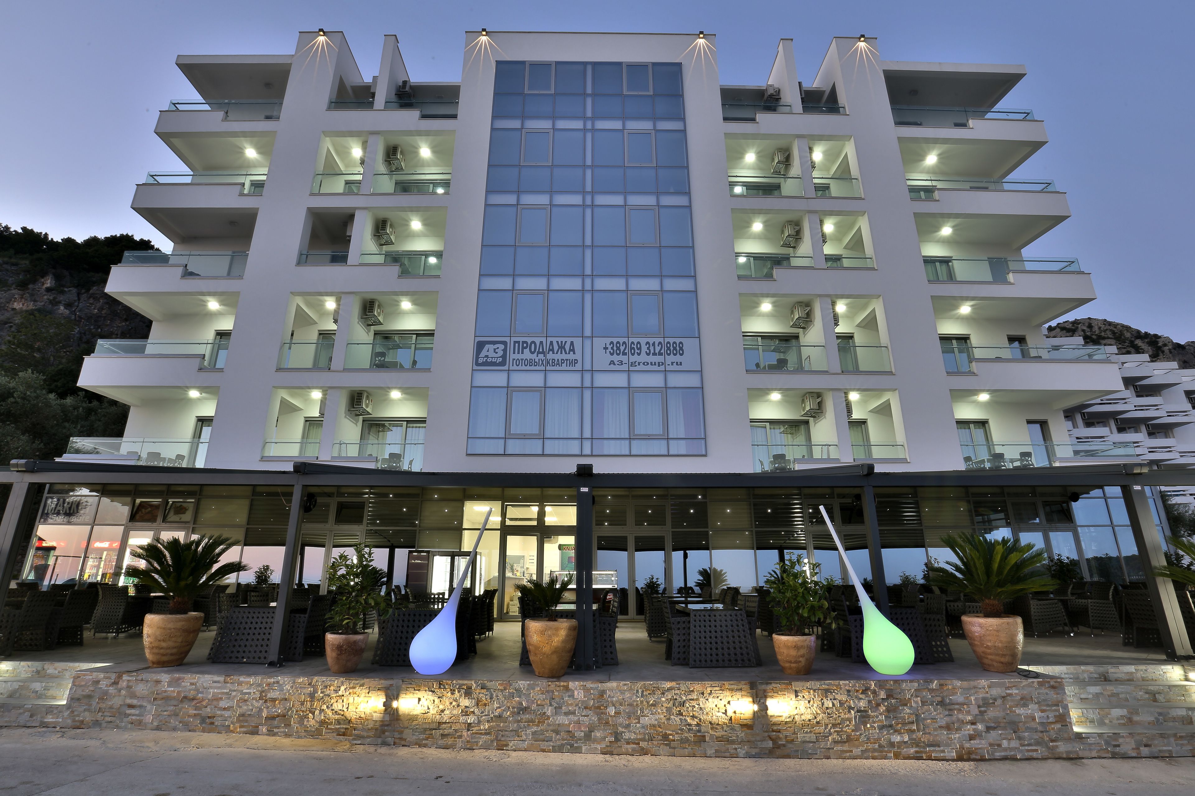 Hotel de vários andares com design moderno, com varandas em cada andar, fachada de vidro e áreas de estar ao ar livre com vasos de plantas.