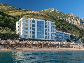 Um hotel moderno com vários andares, localização à beira-mar e muitos guarda-sóis de praia.