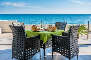 Mesa posta para dois, com toalha verde, duas cadeiras e vista para o oceano.