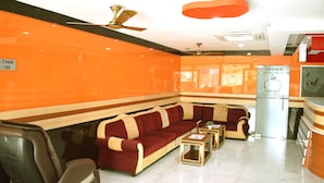 Um saguão de hotel com um conjunto de sofá vermelho e bege, uma mesa de recepção e um ventilador de teto.
