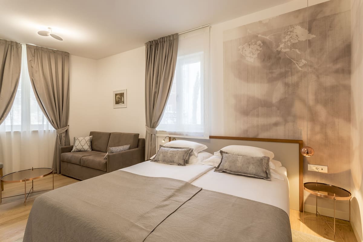 Quarto de hotel moderno com uma cama grande, um sofá, uma mesa redonda e um quadro na parede.