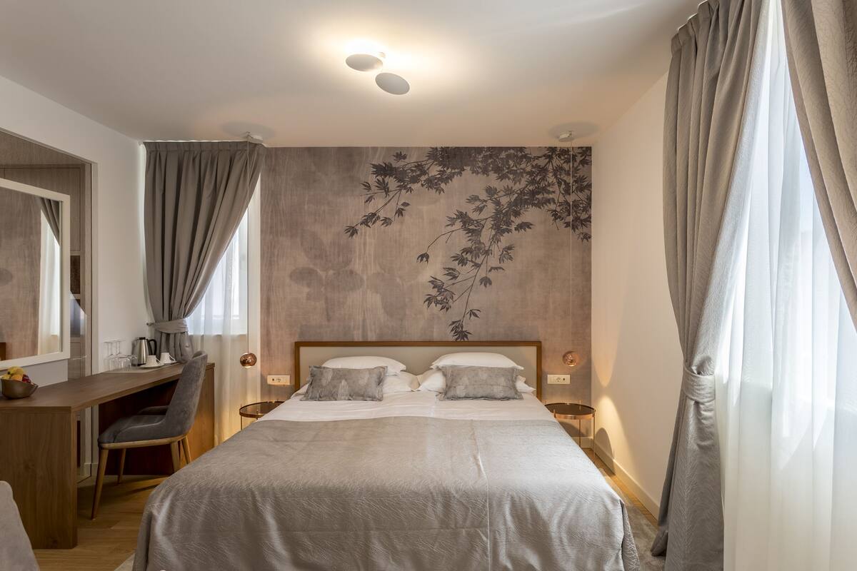 Quarto com uma cama, mesas de cabeceira, escrivaninha e uma cadeira.