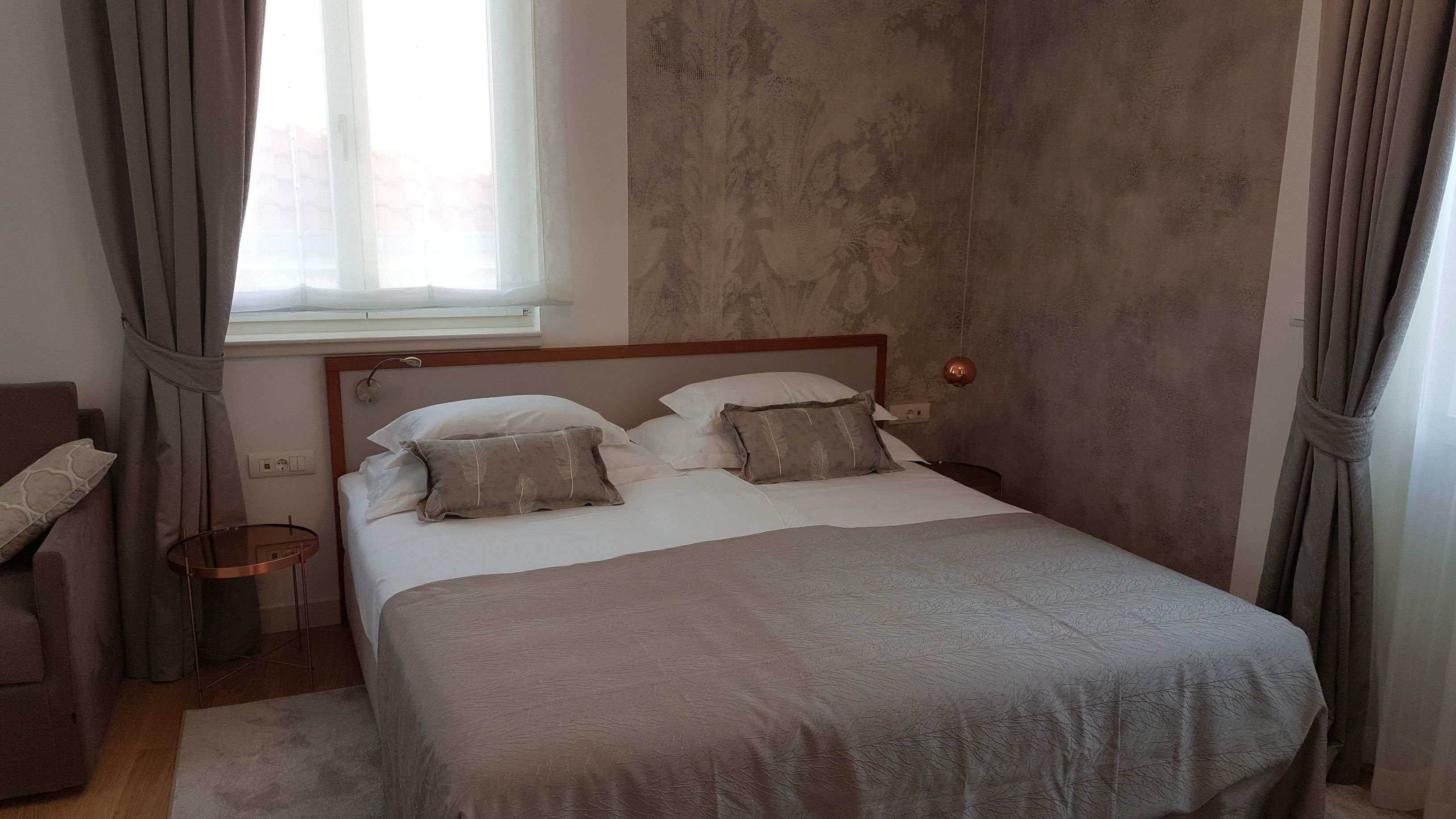 Quarto com uma cama, mesa de cabeceira, cadeira e janela com cortinas.