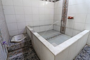 Uma casa de banho com soalho em mosaicos de pedra, sanita branca e cabine de duche com paredes de vidro.