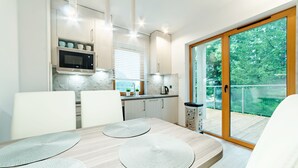 Cozinha moderna com armários brancos, micro-ondas e janela com persianas. Há uma mesa de jantar com jogos americanos e cadeiras.