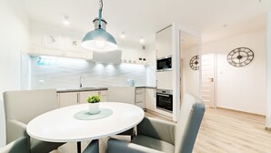 Cozinha moderna com armários brancos, uma mesa de jantar redonda e uma luminária pendente azul.