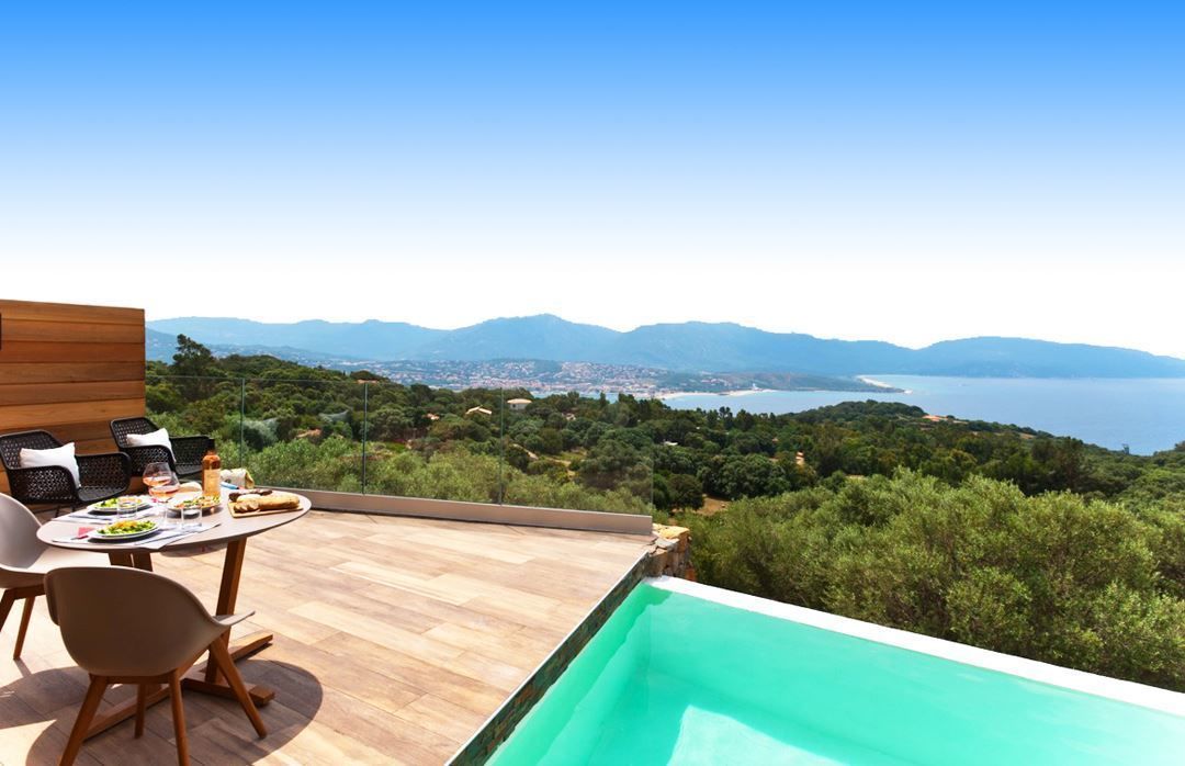 Terraço com piscina, área de refeições e vista panorâmica de montanhas e um lago.