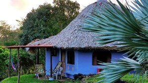 Uma casa azul com telhado de palha, cercada por vegetação exuberante e um caminho de pedra.